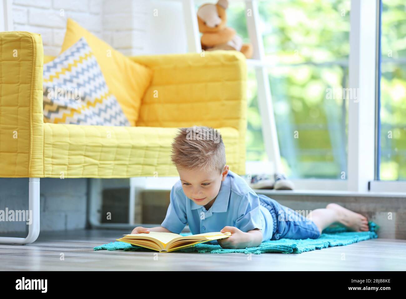 Cute boy reading book on floor in living room Stock Photo - Alamy