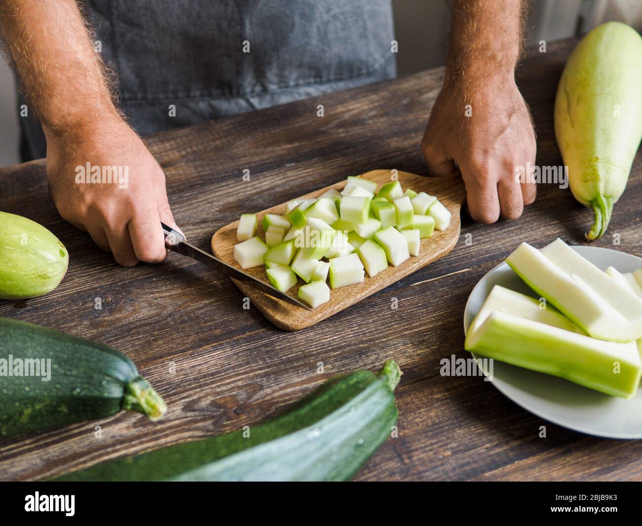 Zucchini harvest. Man slices zucchini cubes for freezing on wooden ...