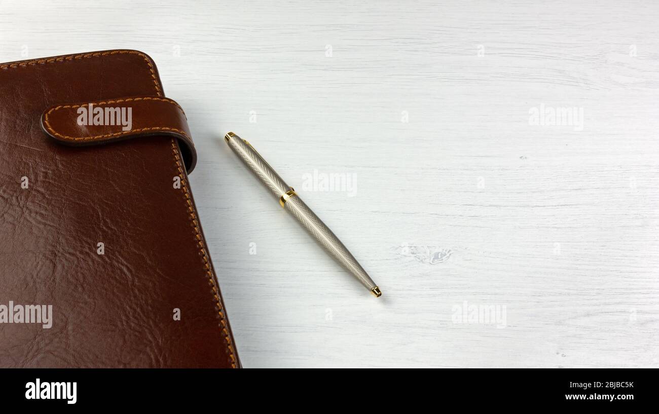 Elegant pen and daily planner with a leather cover on a white wooden ...
