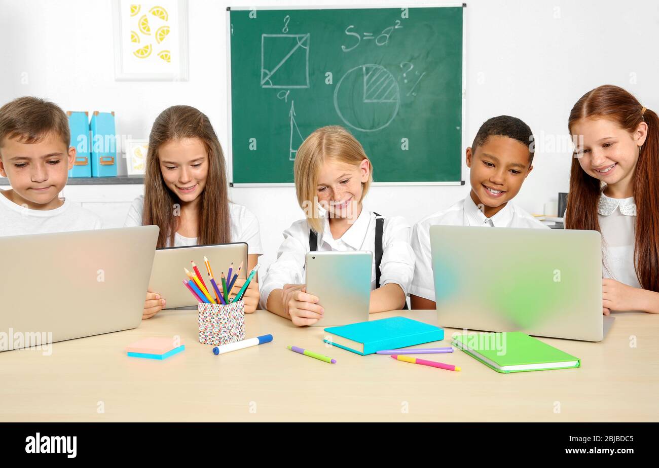 Schoolchildren sitting in classroom with laptops and tablet computers ...