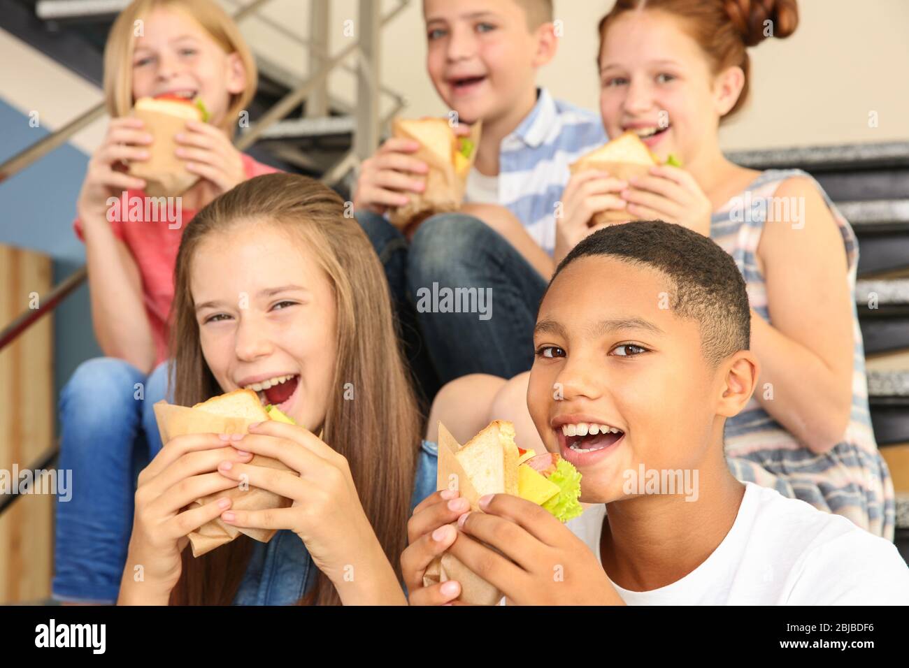 Schoolchildren eating sandwiches while sitting on stair-steps at school ...