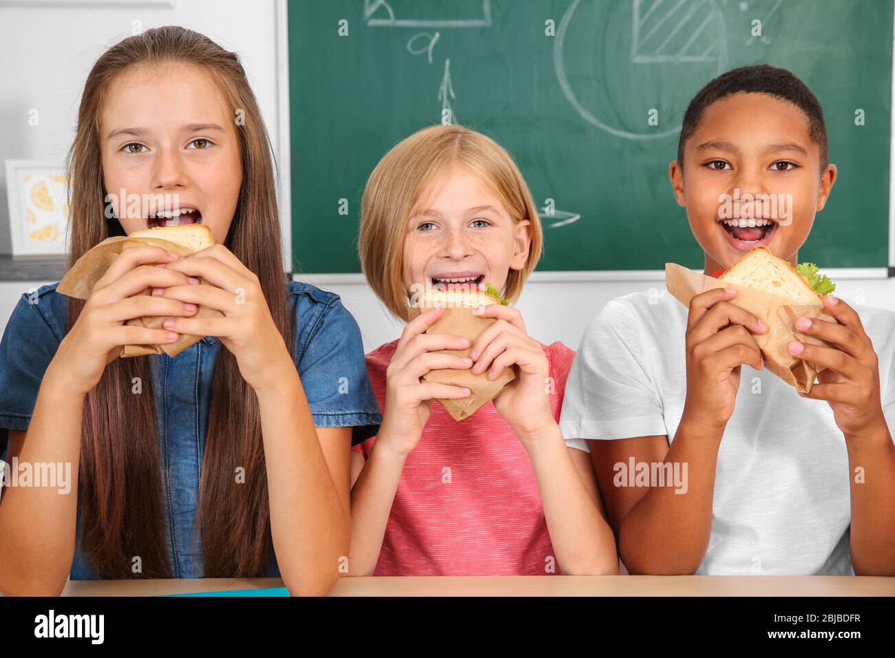 Schoolchildren having lunch in classroom Stock Photo - Alamy