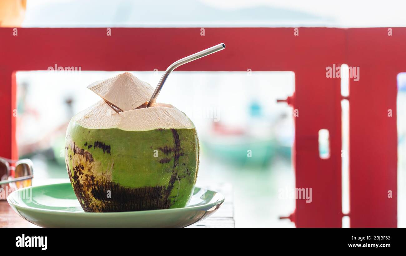 Fresh and cold whole coconut served with cut top and straw inside in ...