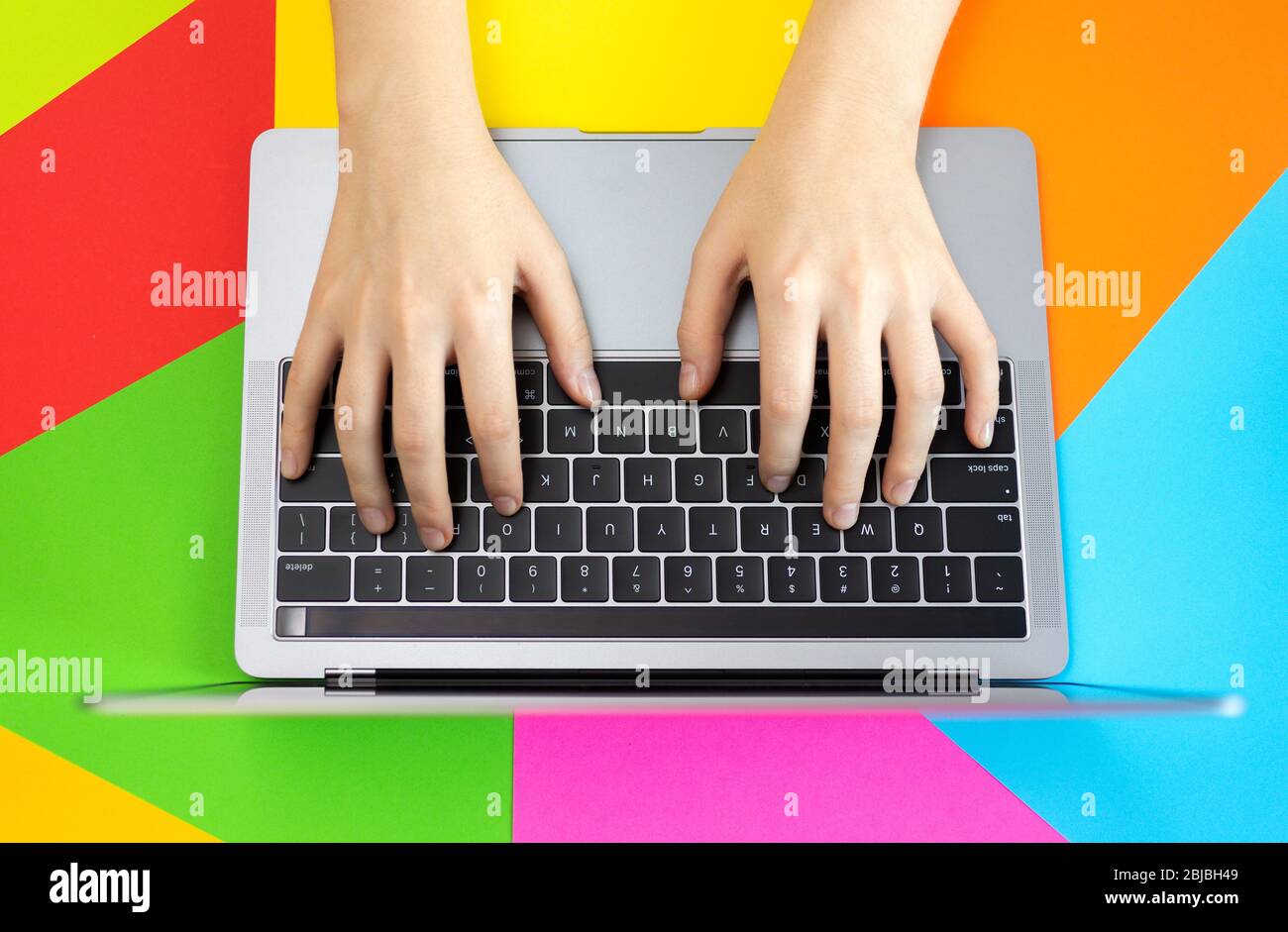 Top view of hands on laptop keyboard, colorful background. Workplace ...
