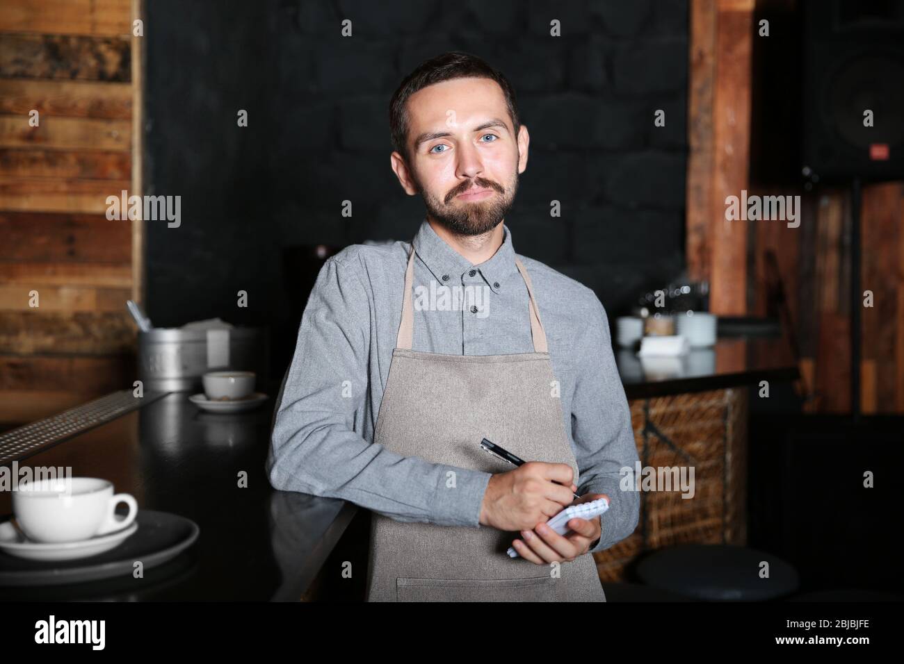 Bartender with notebook and pen standing near wooden bar counter Stock ...