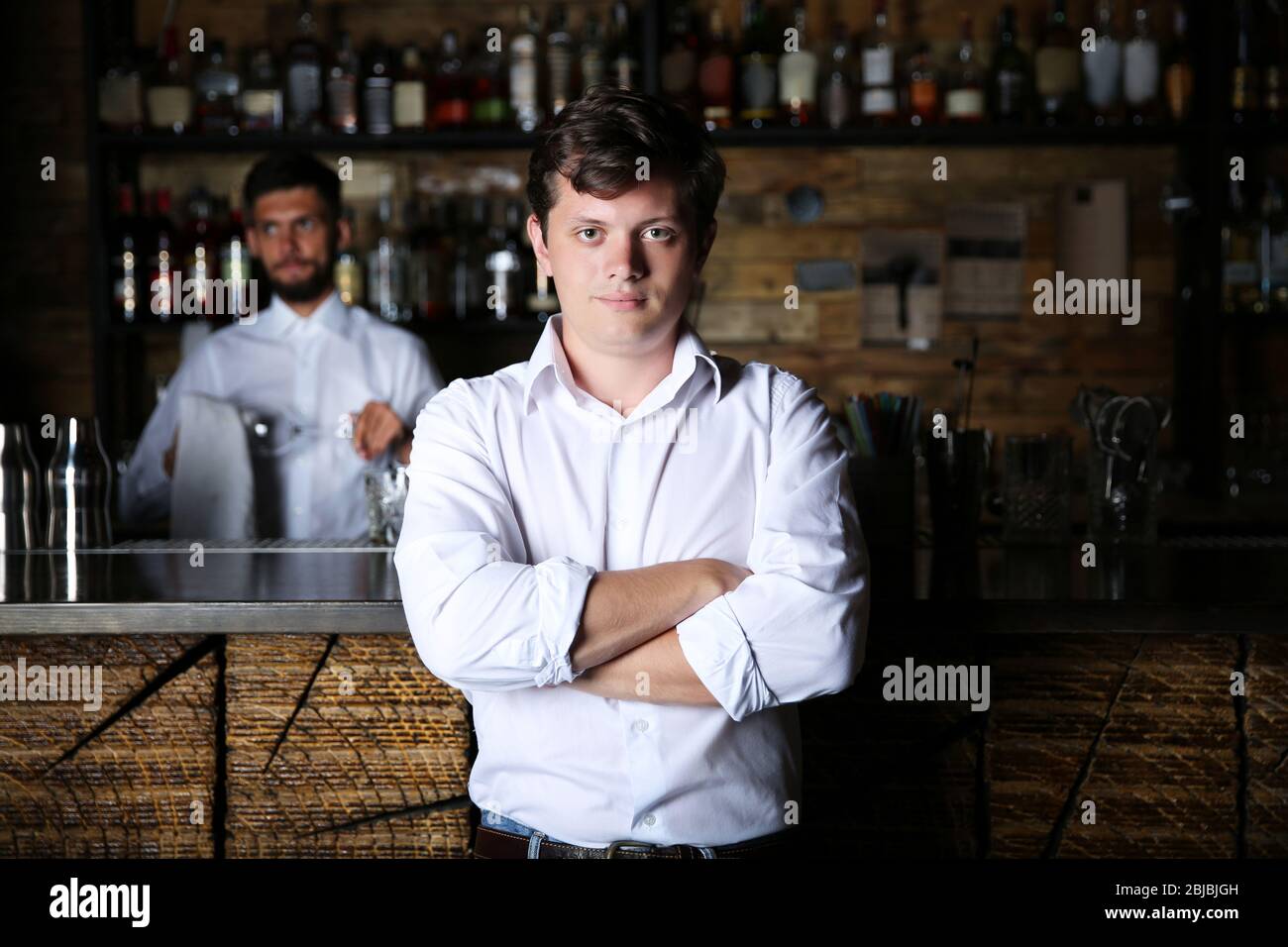 Man with crossed arms standing near wooden bar counter Stock Photo - Alamy