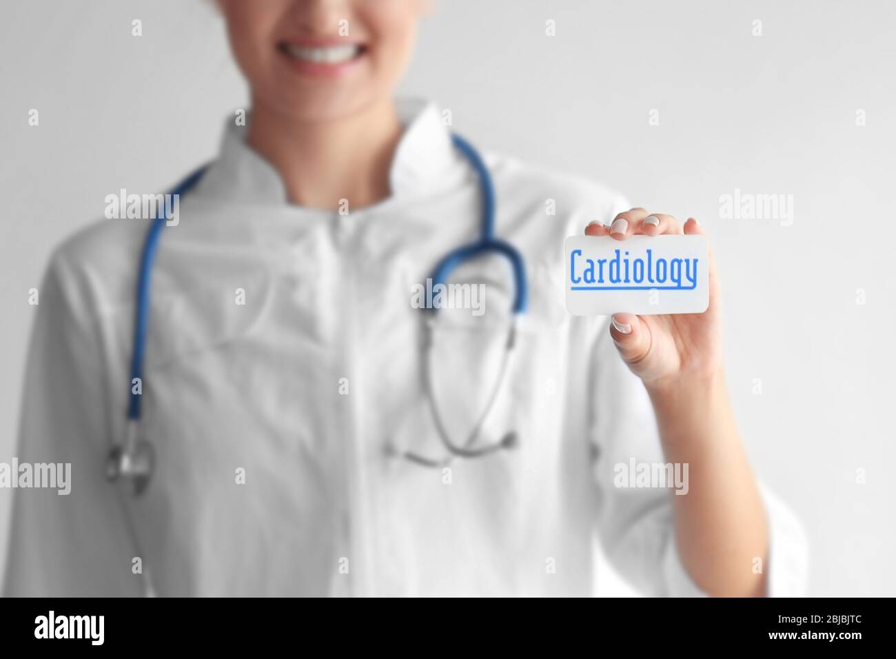 Doctor holding card with word CARDIOLOGY on white wall background Stock ...