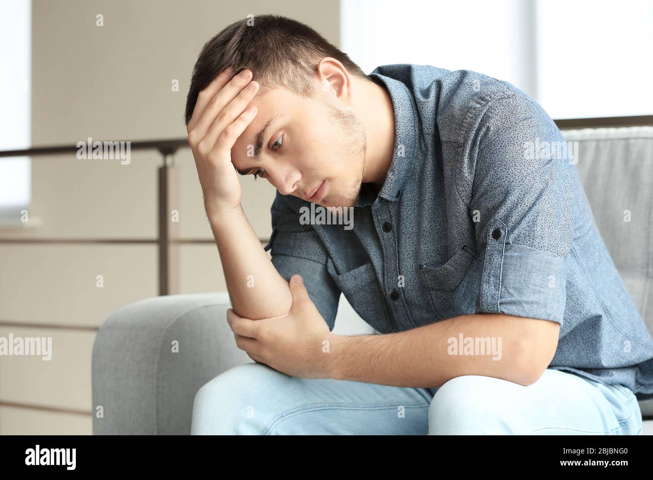 Young worried man sitting on couch at home Stock Photo - Alamy