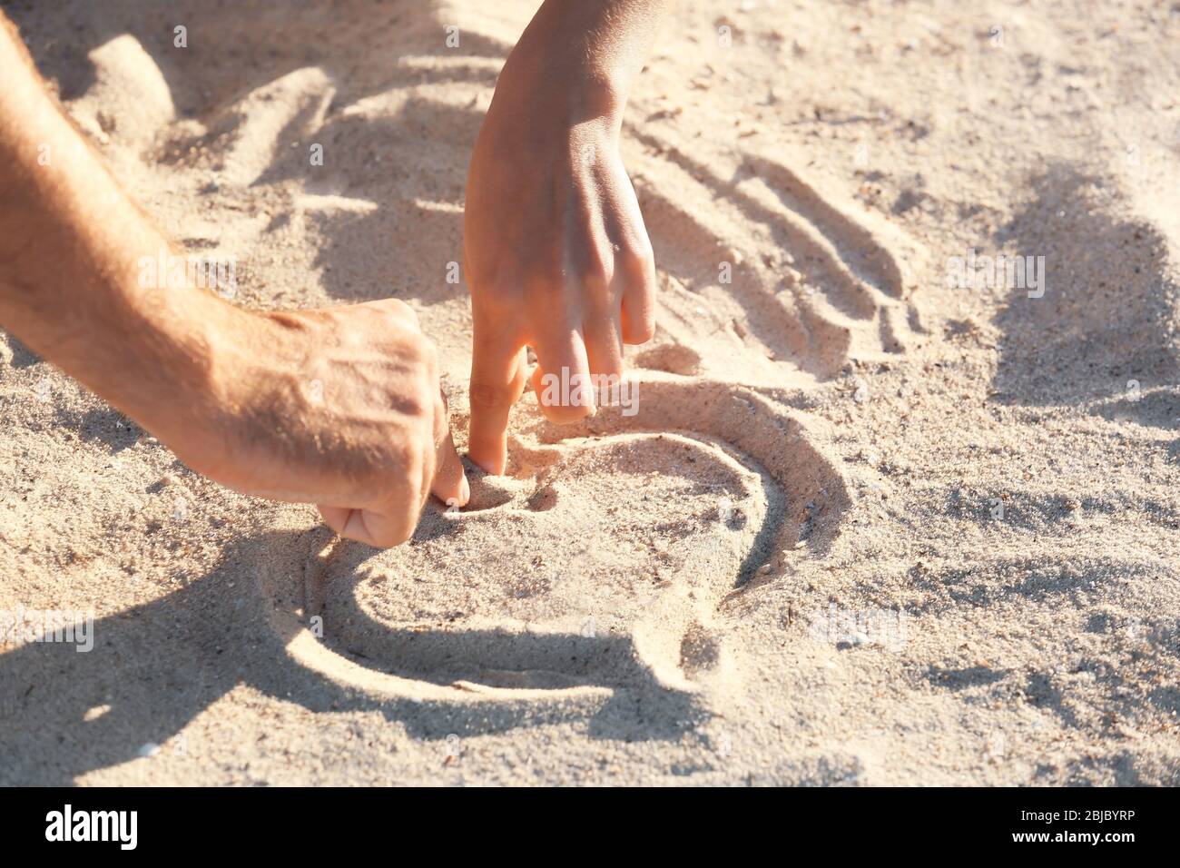 Two hands drawing heart on sand, closeup Stock Photo - Alamy