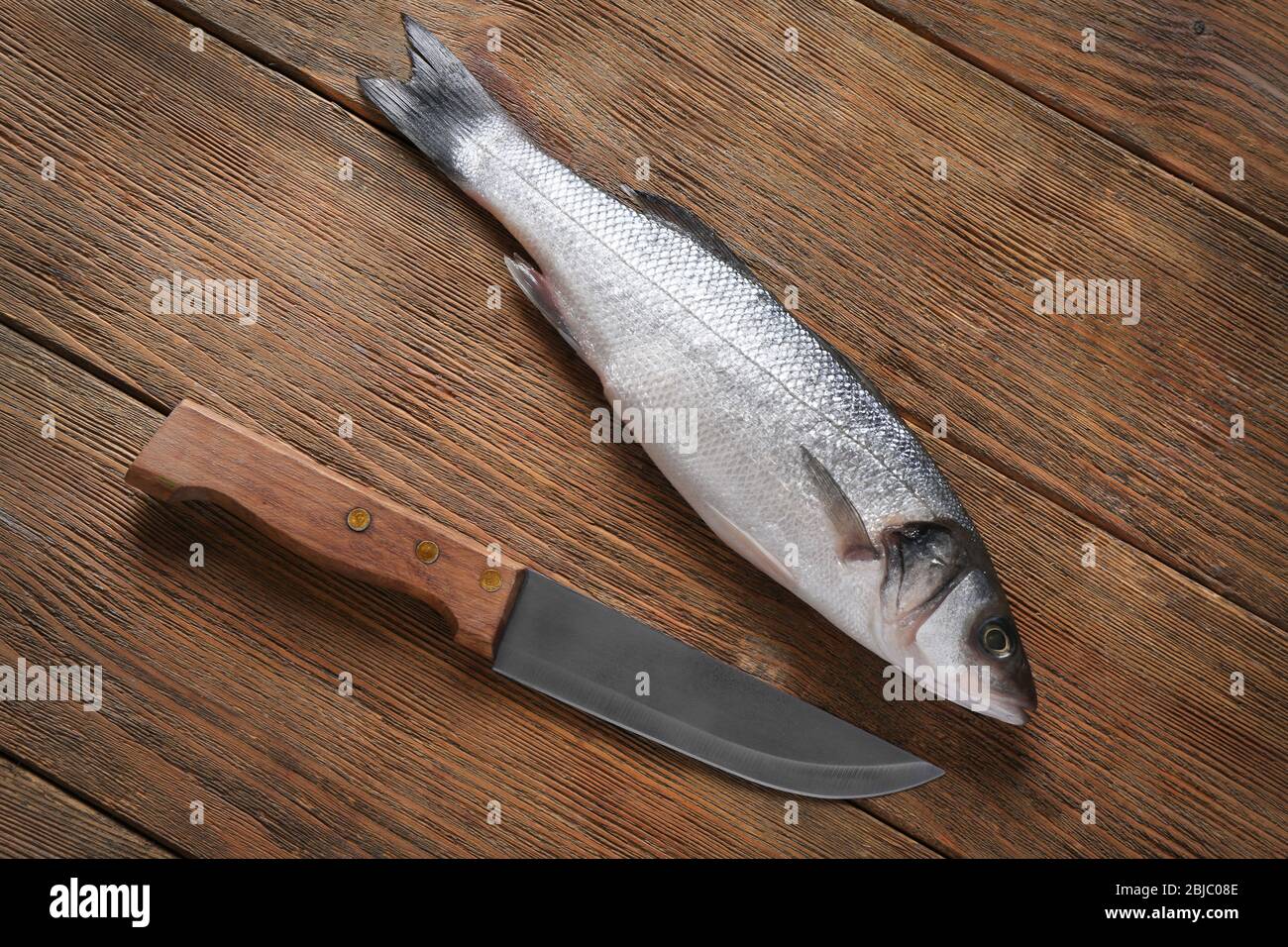 Raw fish with knife on kitchen table Stock Photo - Alamy