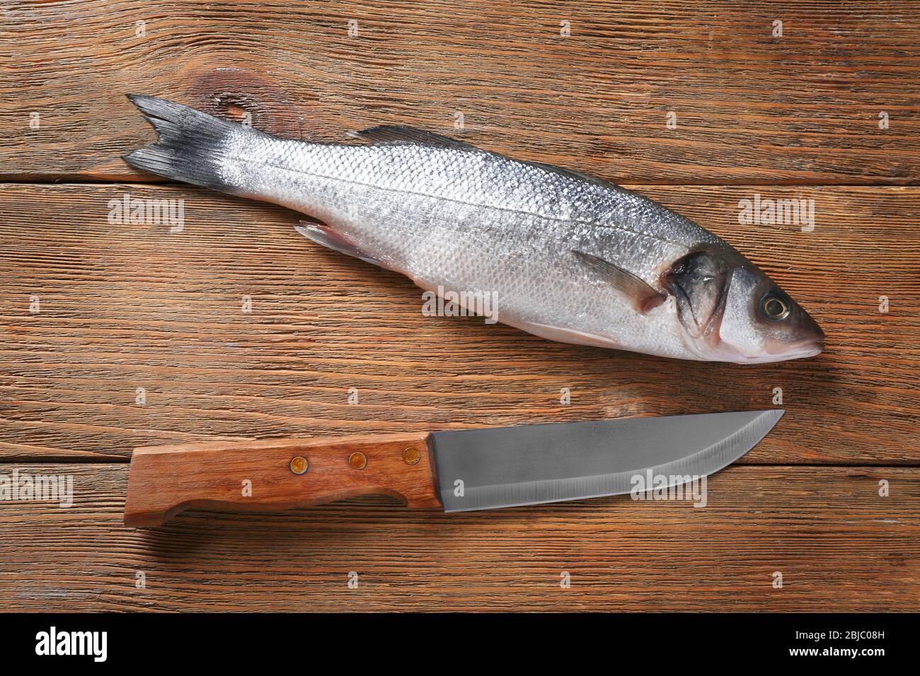 Raw fish with knife on kitchen table Stock Photo - Alamy
