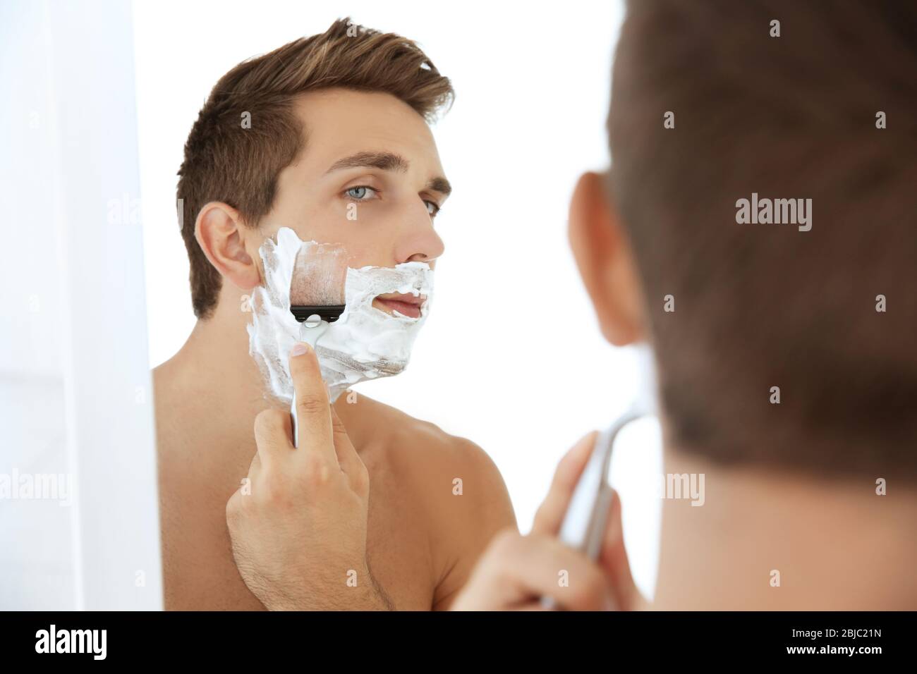 Young handsome man shaving his face in bathroom Stock Photo - Alamy