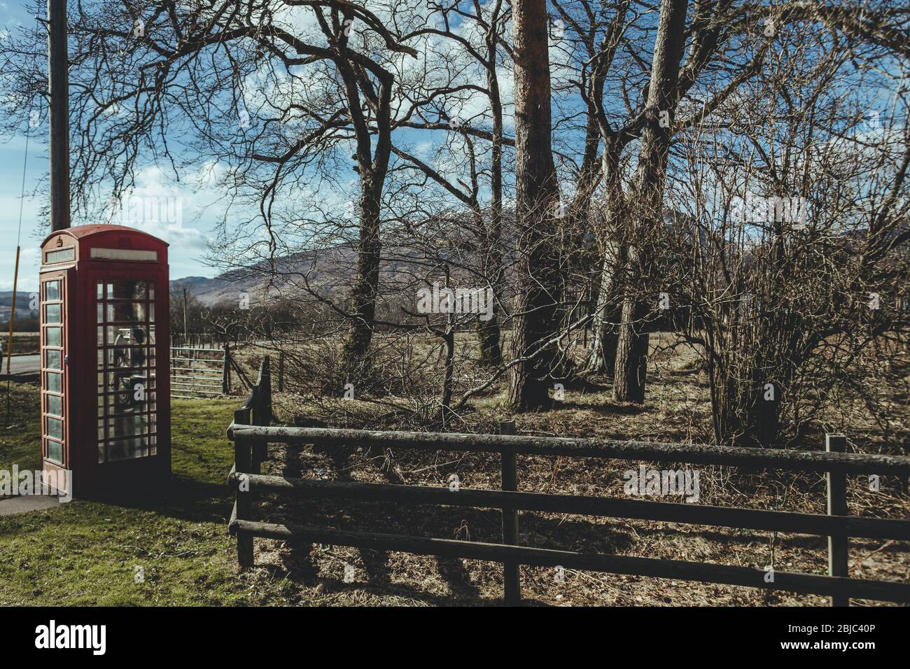 Traditional red telephone box on a side of a road near wooden fence in ...