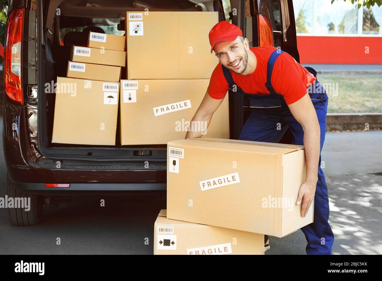 Delivery man unloading parcel from car Stock Photo - Alamy