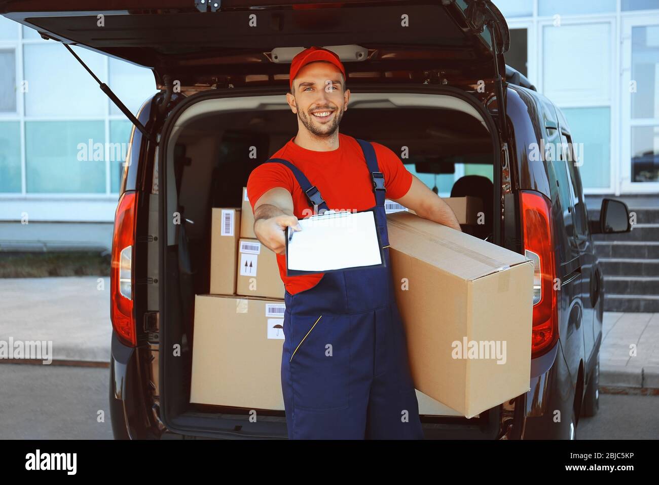 Delivery man holding package stretching clipboard Stock Photo - Alamy