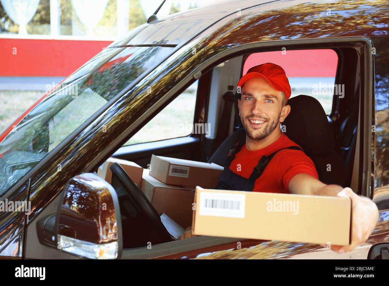 Delivery man with parcel in car Stock Photo - Alamy