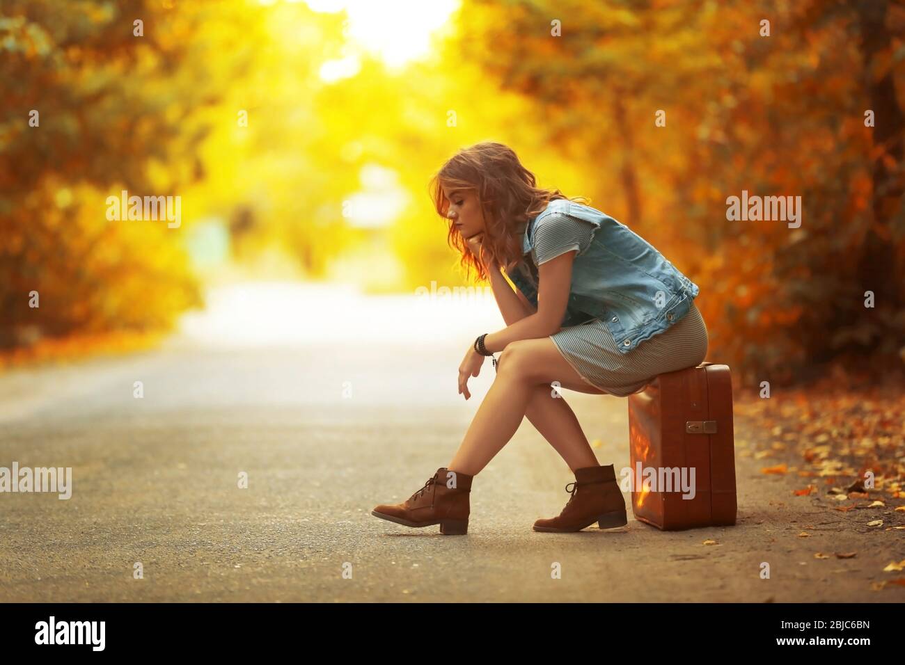 Beautiful young woman sitting on suitcase Stock Photo - Alamy