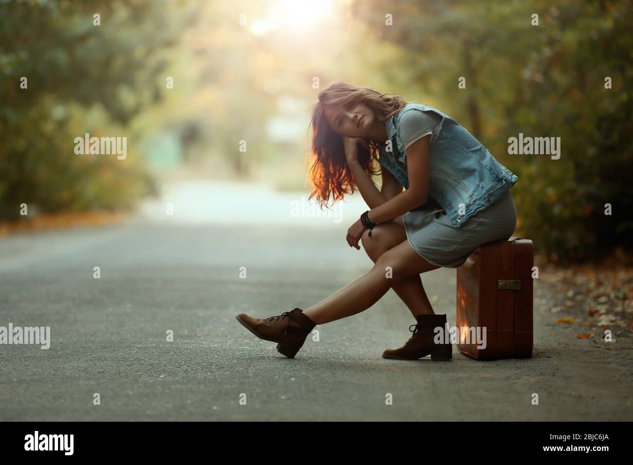Beautiful young woman sitting on suitcase Stock Photo - Alamy