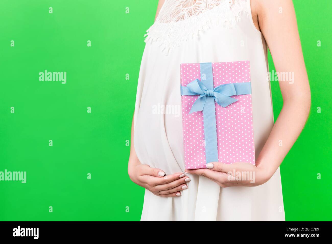 Cropped image of pink spotted gift box in pregnant woman's hand against ...