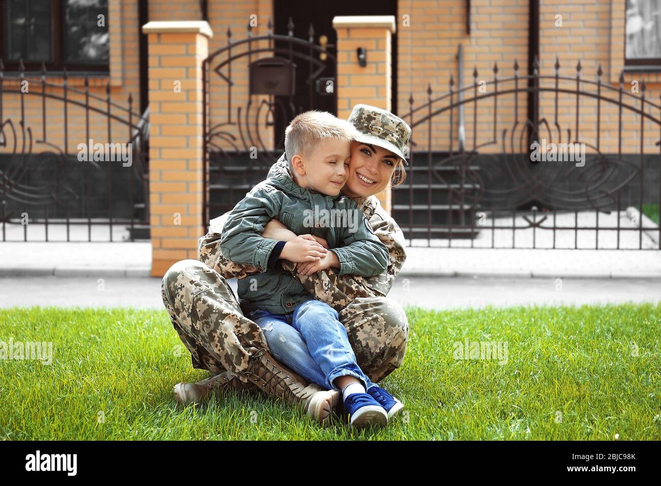 Mother soldier with kid embracing and sitting on green grass Stock ...