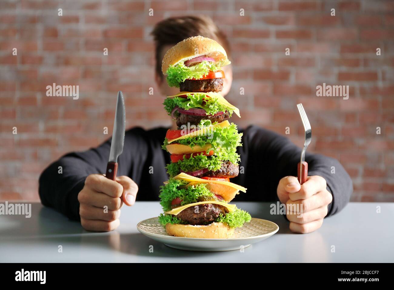 Man eating huge burger at table Stock Photo - Alamy