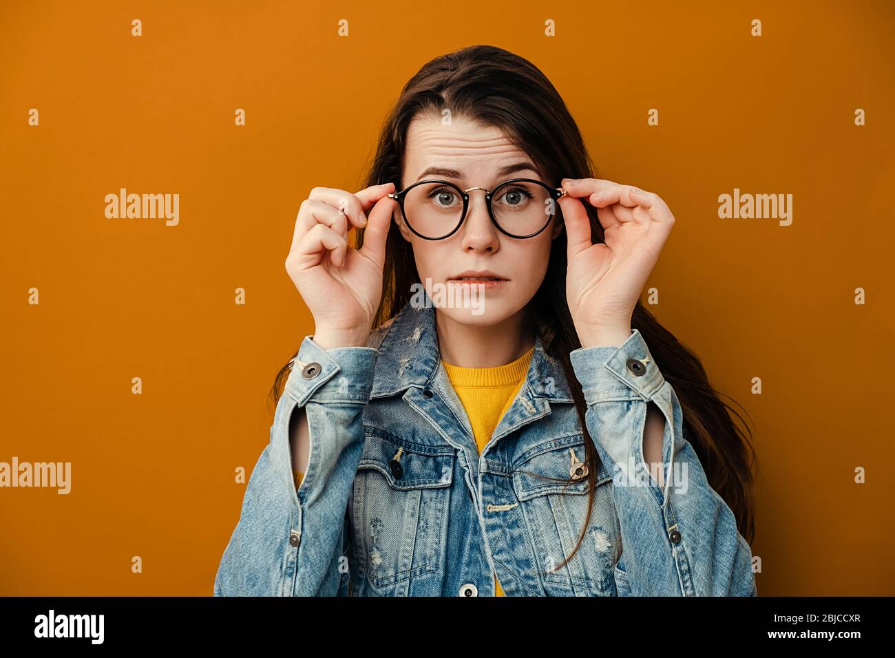 Portrait of shocked woman keeps hands on rim of spectacles looks with ...