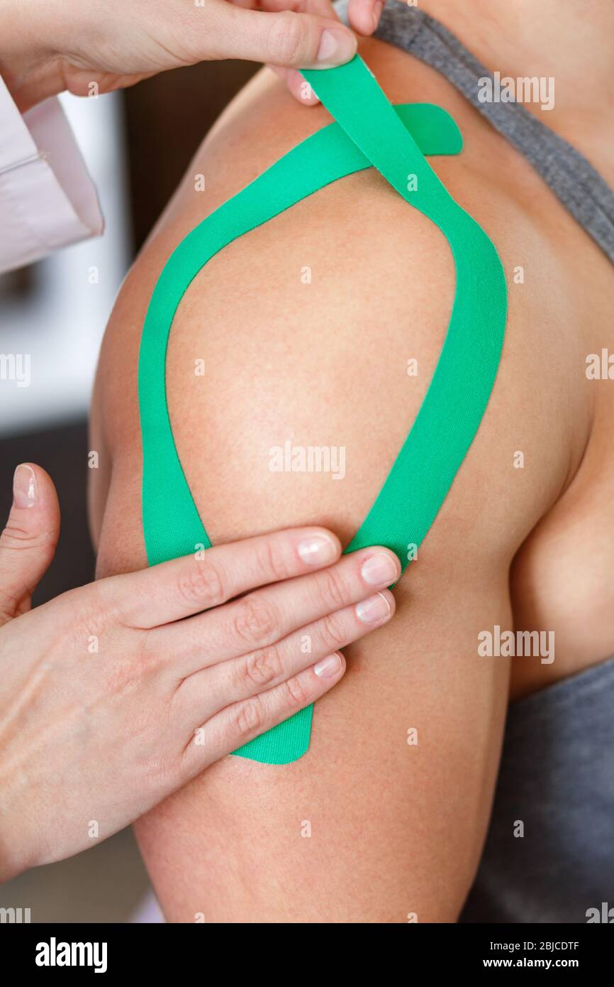 Kinesiology taping. Physical therapist applying kinesiology tape to patient shoulder. Female ...