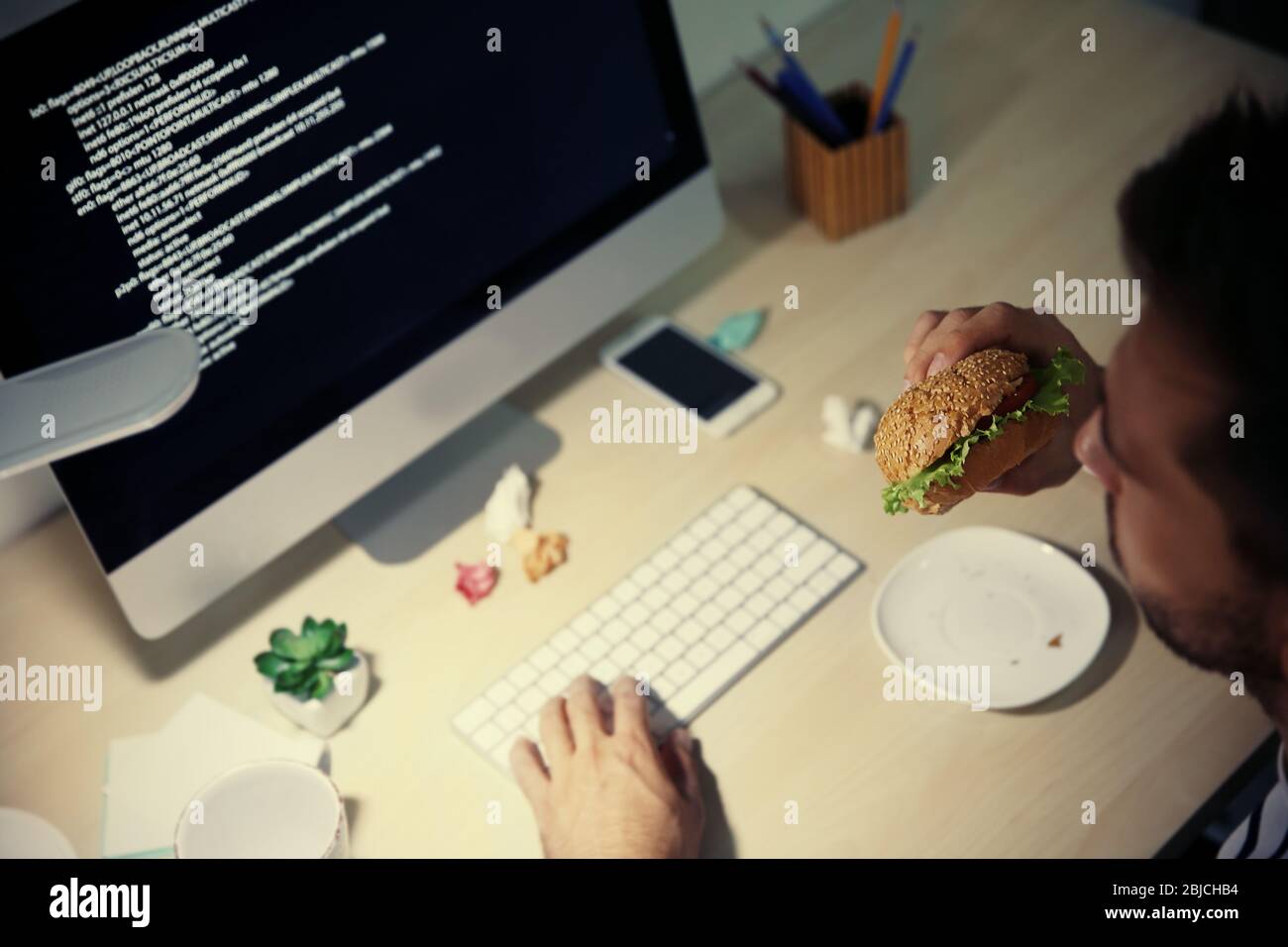 Man having snack while working with computer late in evening, close up ...