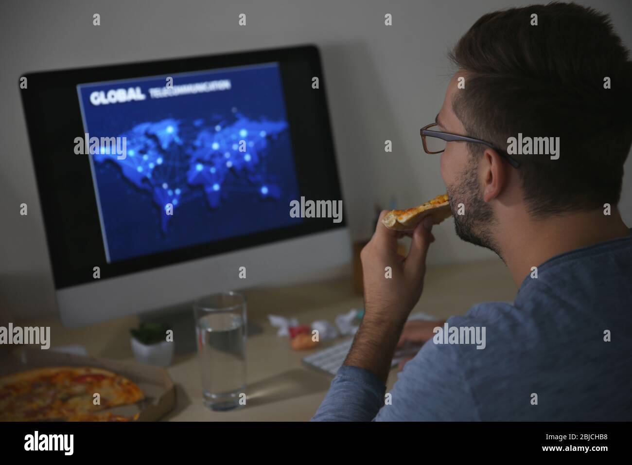 Man eating pizza while working with computer late in evening, close up ...