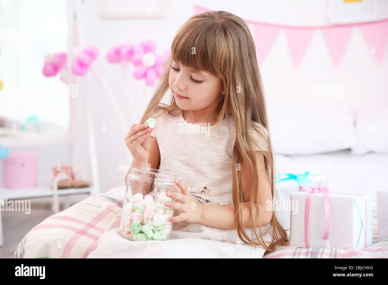 Cute birthday girl eating sweets while sitting on bed at home Stock ...