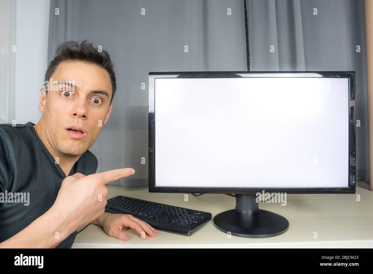 Surprised man in black shirt pointing at a computer screen (space copy ...