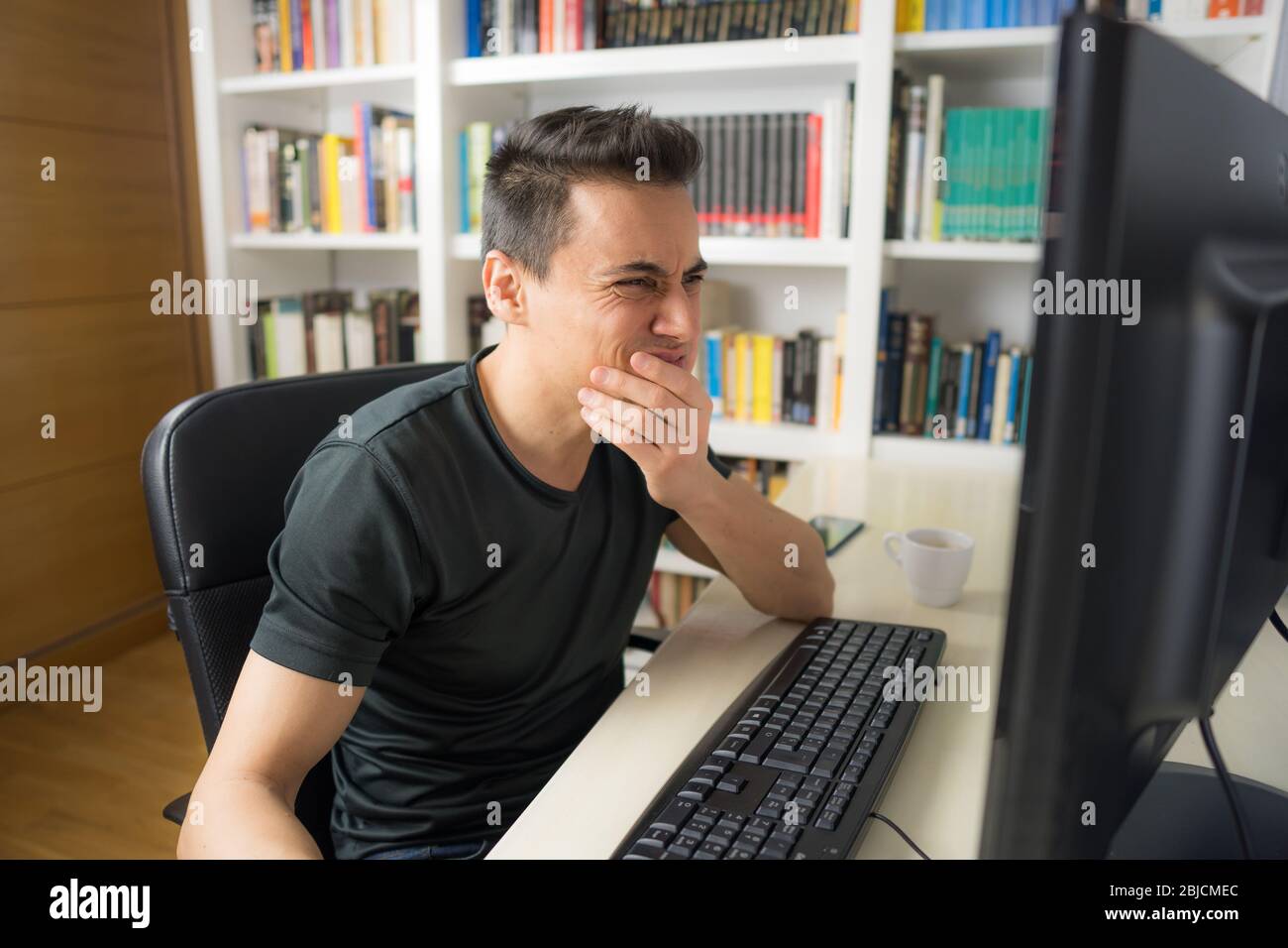 Man sitting in front of the computer in a shirt showing concern and ...