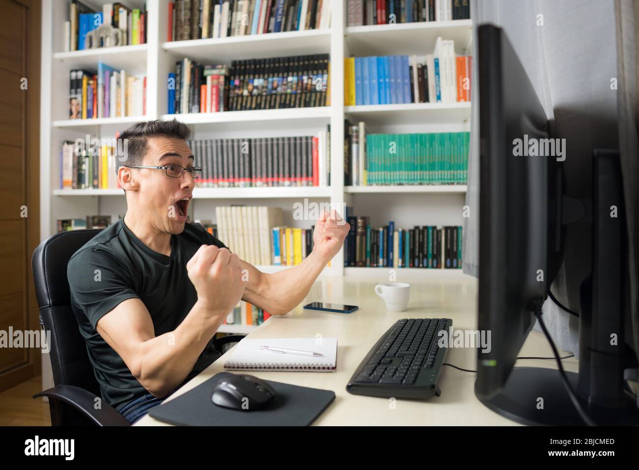 Smiling and happy man in his room sitting at the computer looking at ...