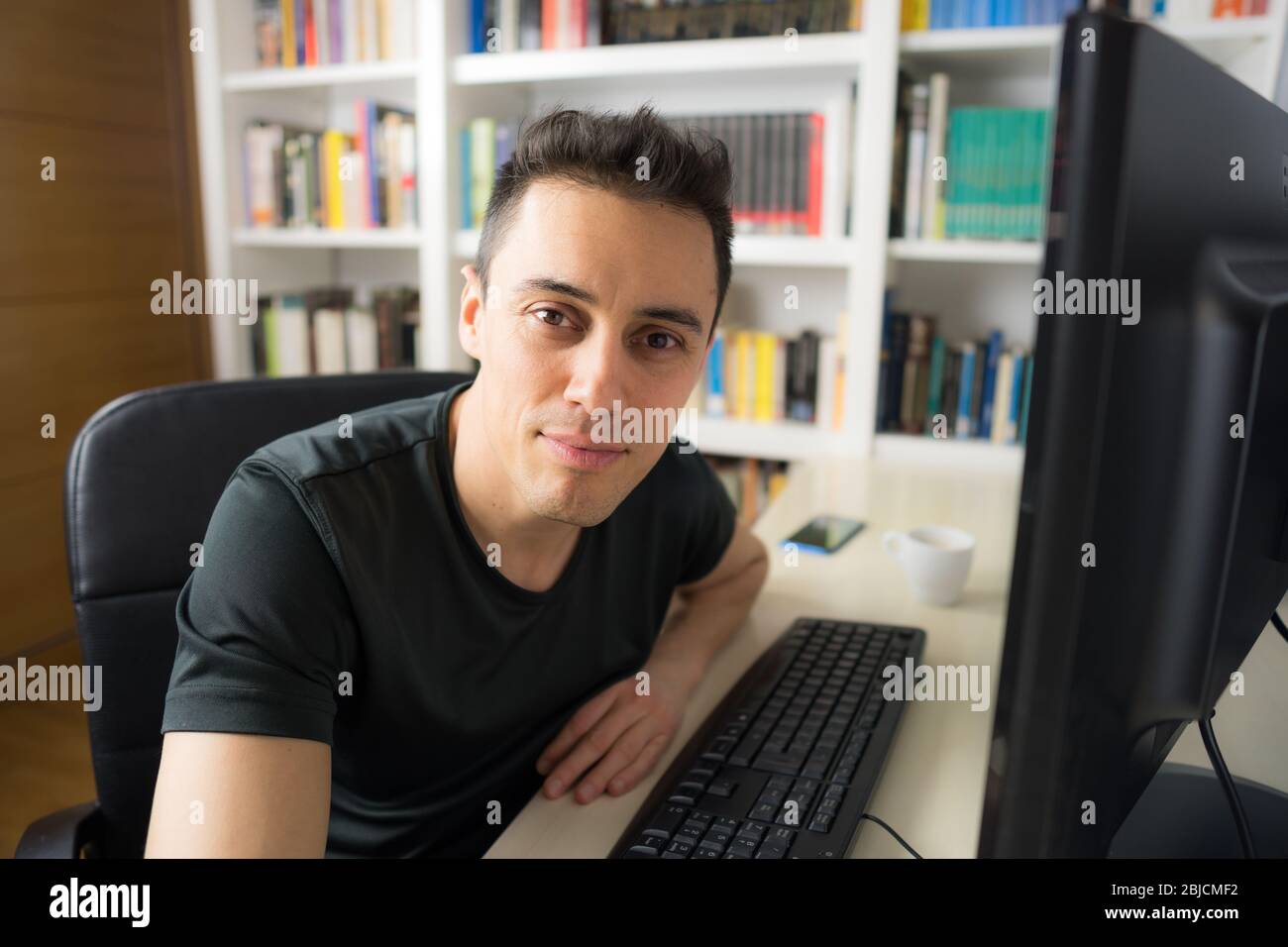 Smiling and happy man in his room sitting at the computer looking at ...