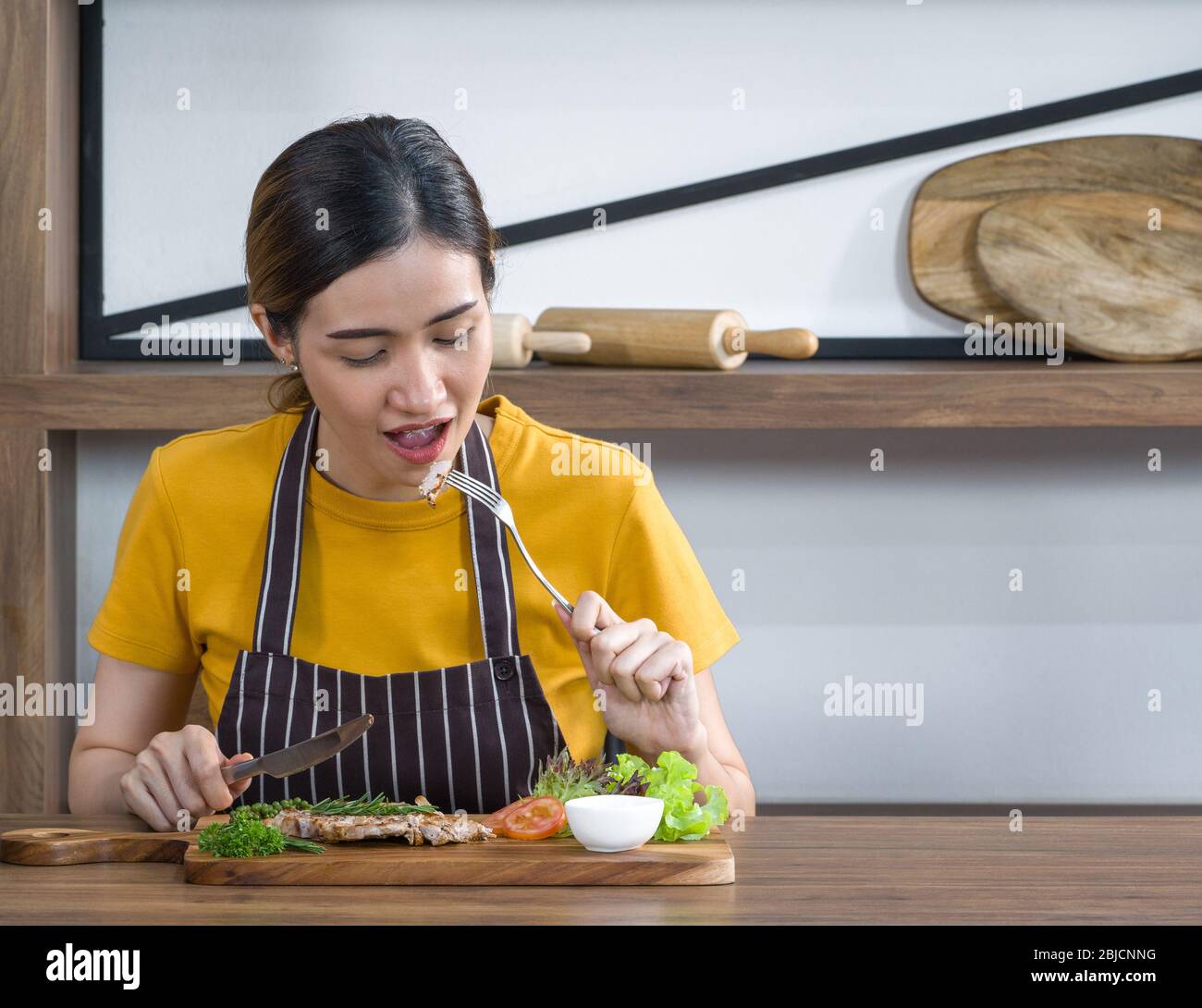 The housewife dressed in an apron enjoy eating the delicious steak ...