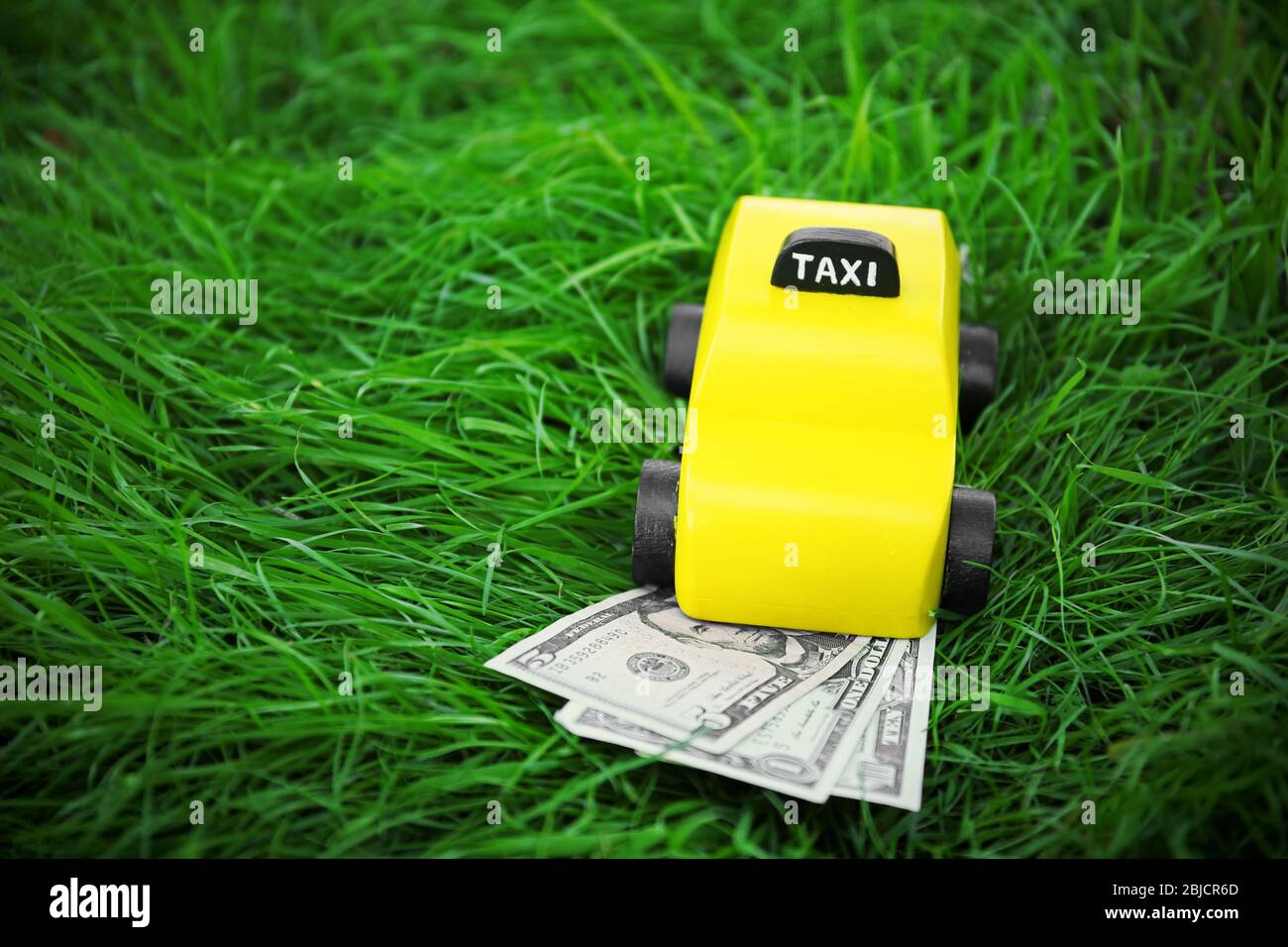 Yellow toy taxi with money on green grass Stock Photo - Alamy