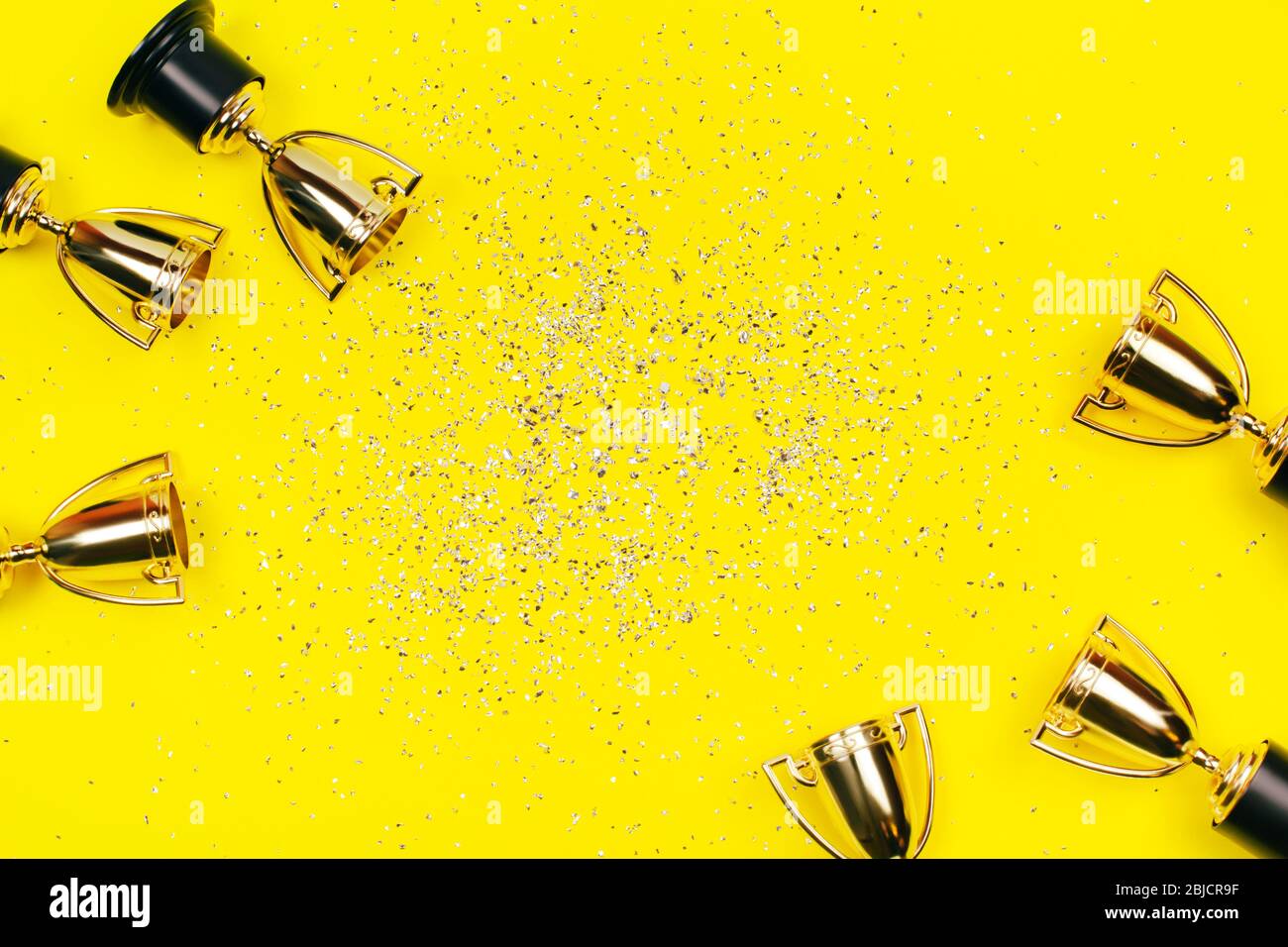 Golden winner cups with silver sparkles on a yellow background with ...