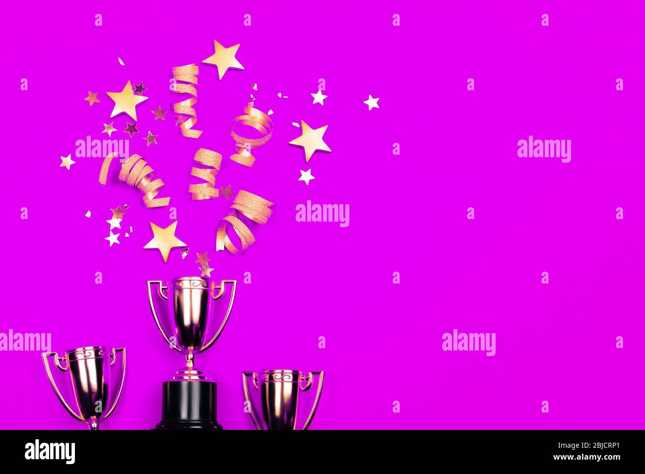 Three golden winner cups with confetti on a purple background. Flat lay ...