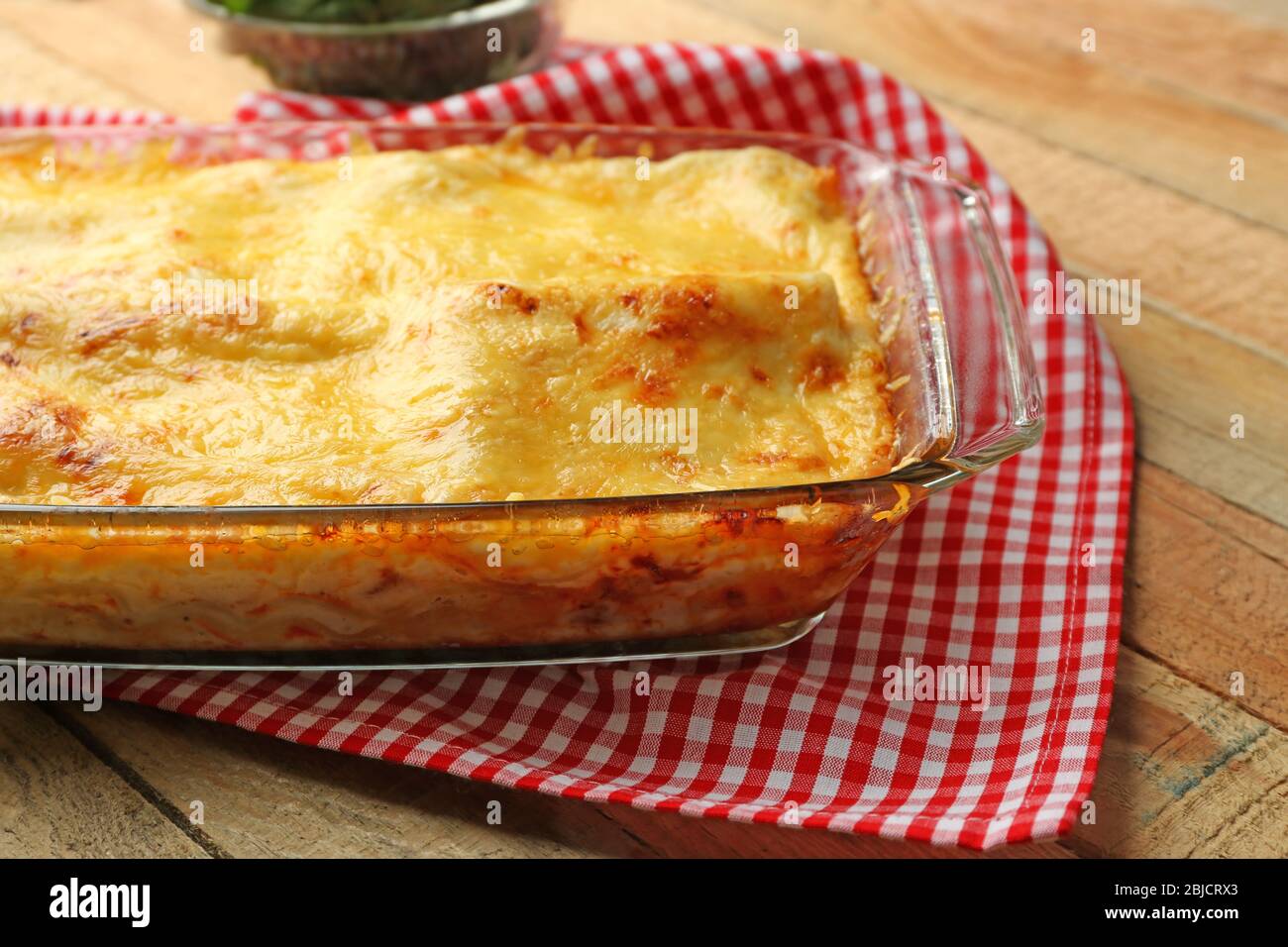 Traditional lasagna in glass baking dish and napkin on wooden table ...