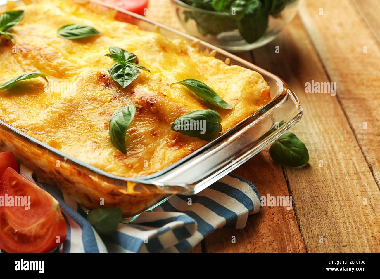 Traditional lasagna in glass baking dish and tomatoes on wooden table ...
