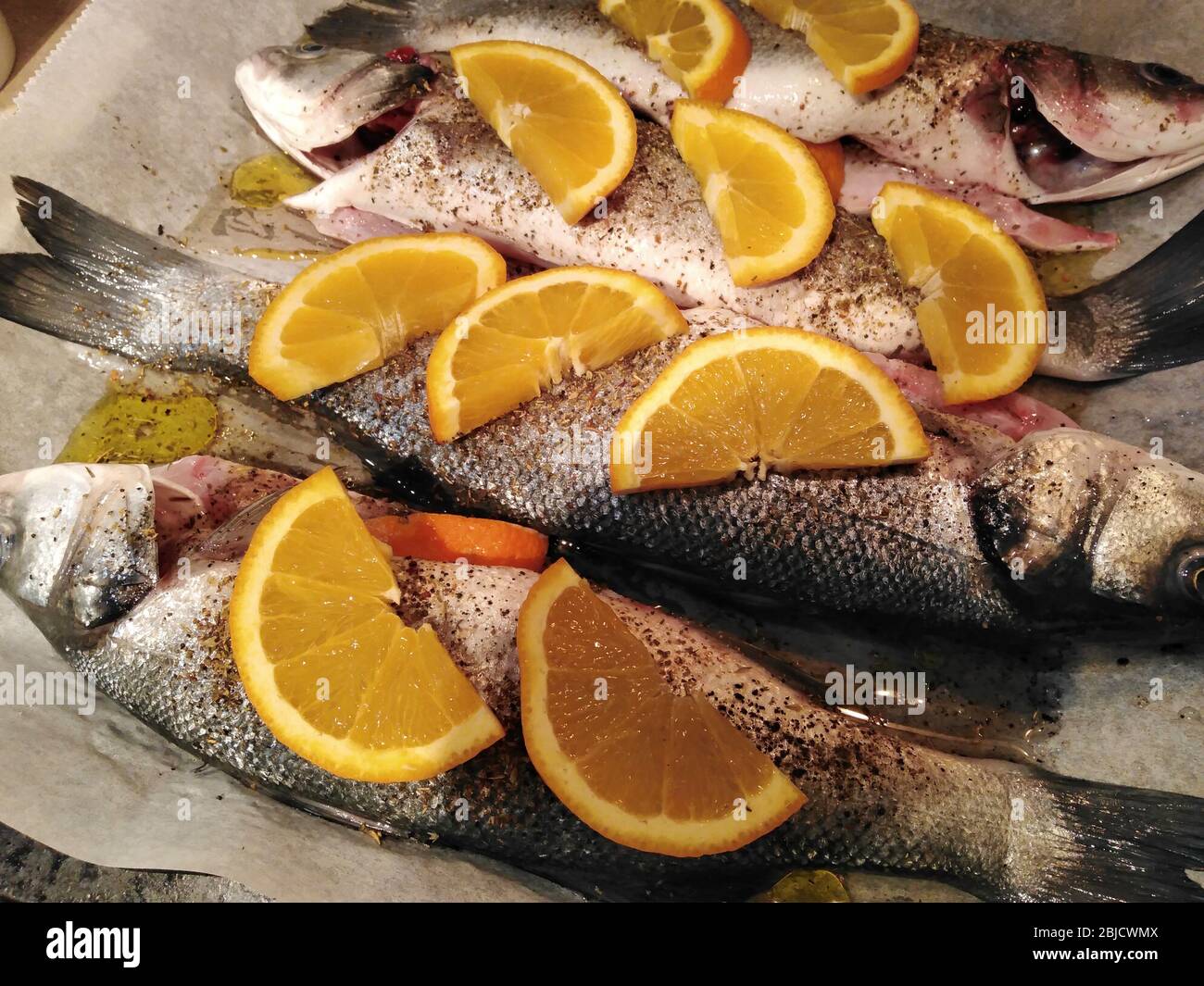 Sea bass with slices of orange in sheet pan prepared for baking in oven ...