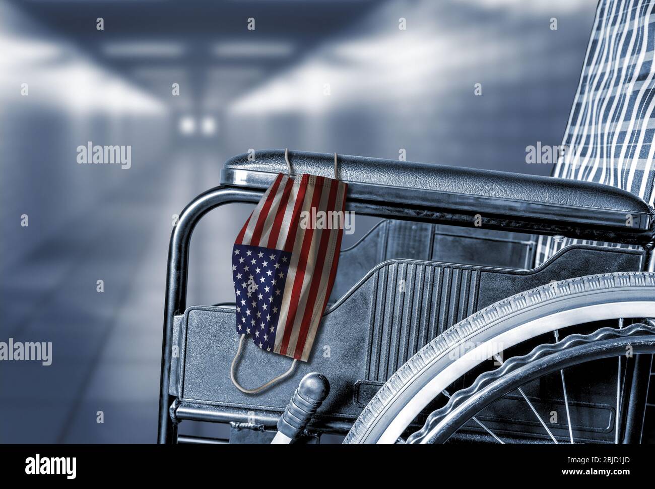 Flag of United States on face mask hanging on empty wheelchair in hallway of American hospital ...