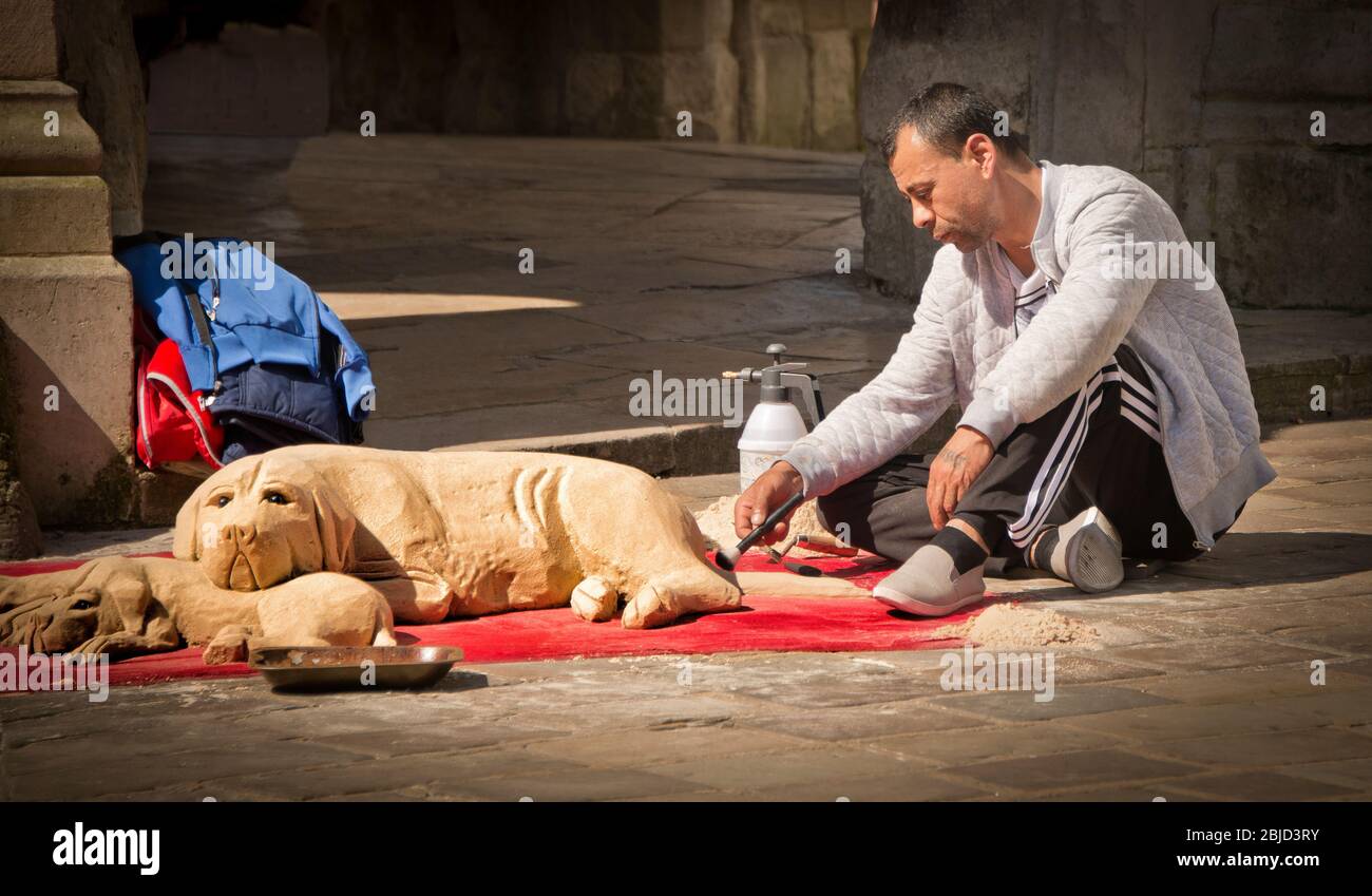 Man finishing sand sculpture of a golden coloured dog on pedestrian ...