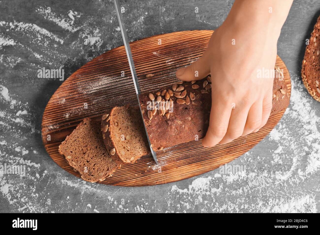 Female hand cutting rye bread with seeds on grey table background Stock ...
