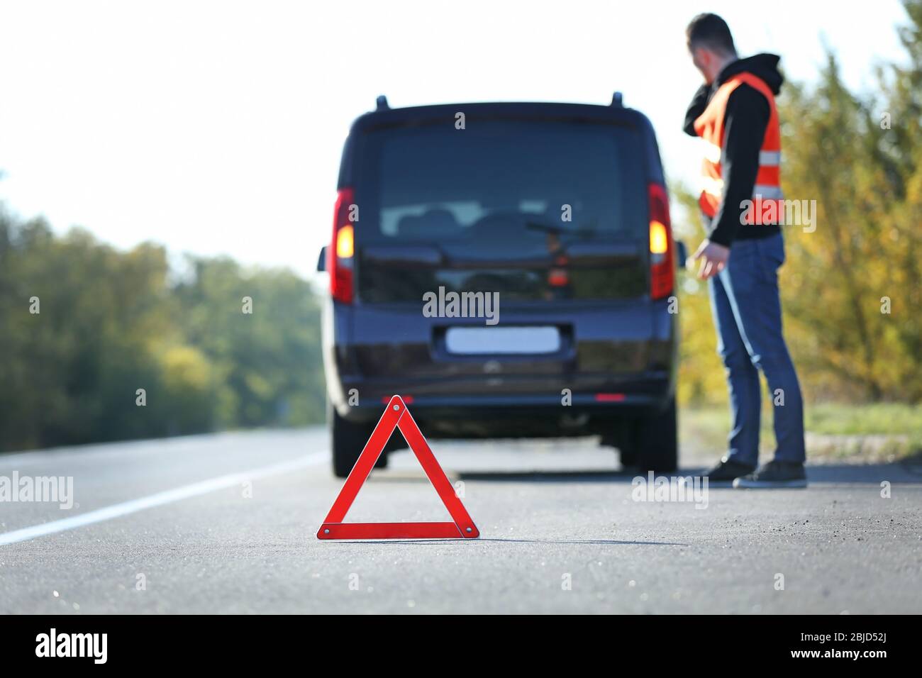 Red warning triangle on asphalt road. Tow truck worker near broken down ...