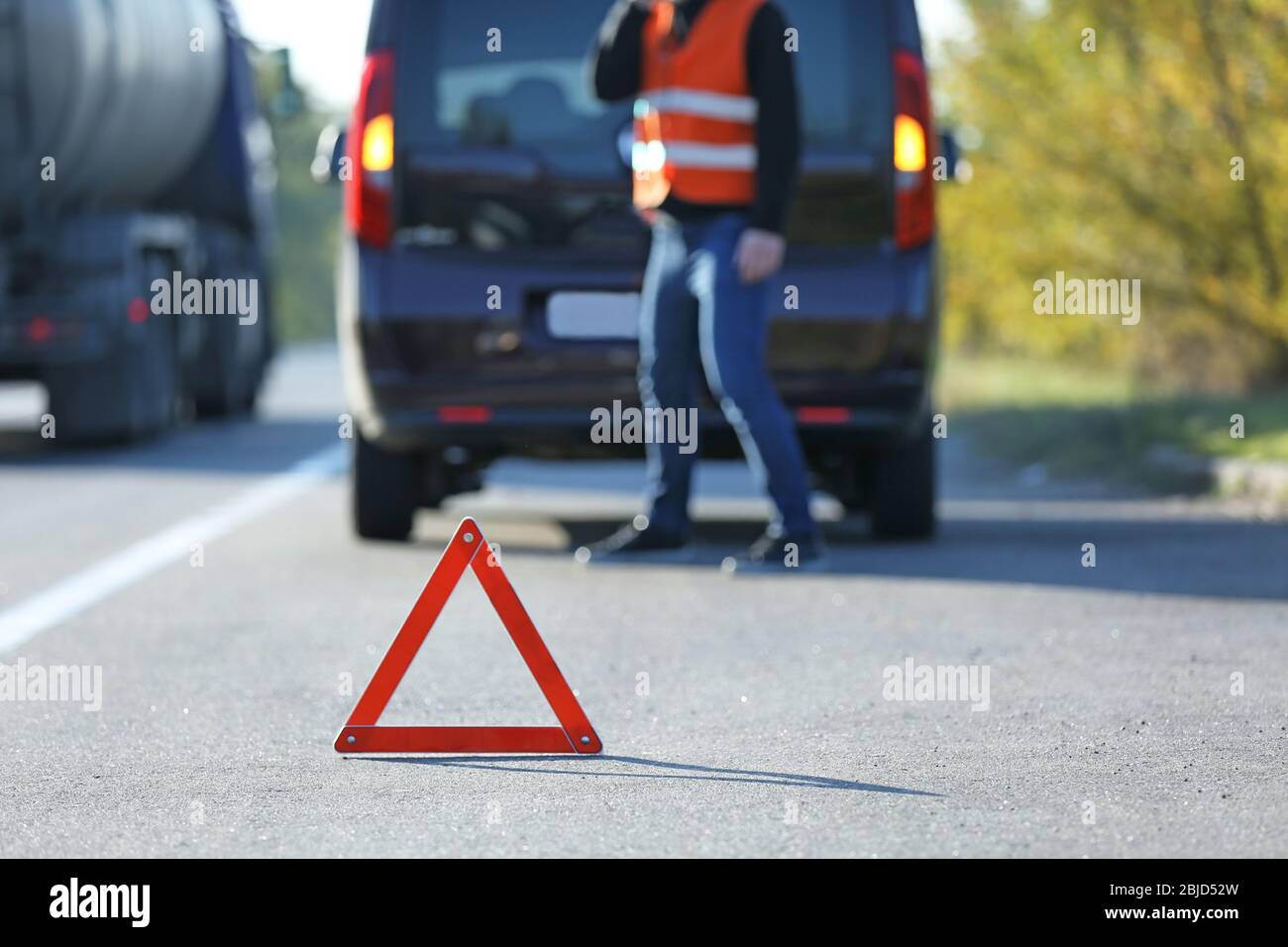 Red warning triangle on asphalt road. Tow truck worker near broken down ...