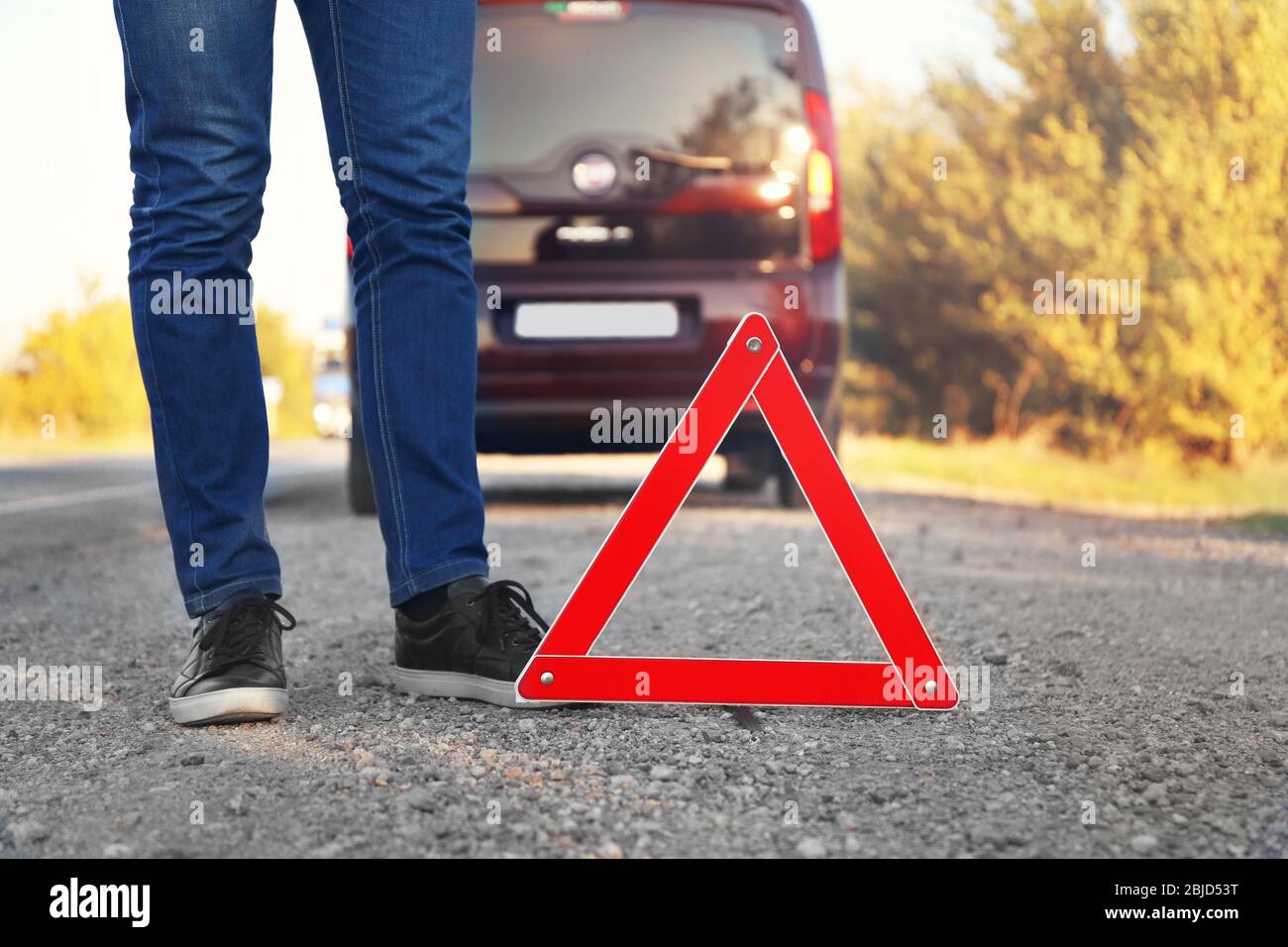 Legs of driver standing near red warning triangle on asphalt road ...