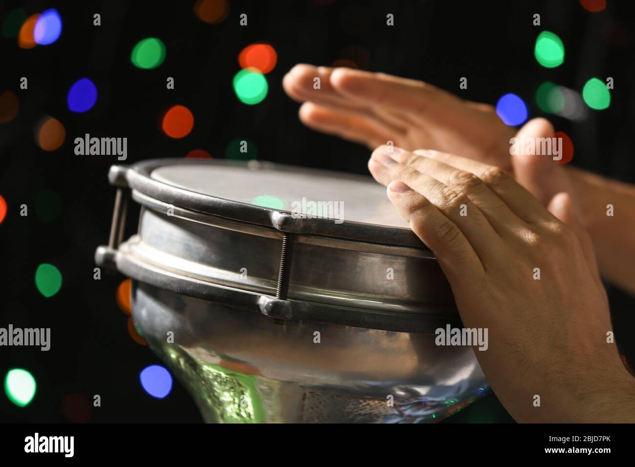 Hands of man playing African drum against defocused lights, close up ...