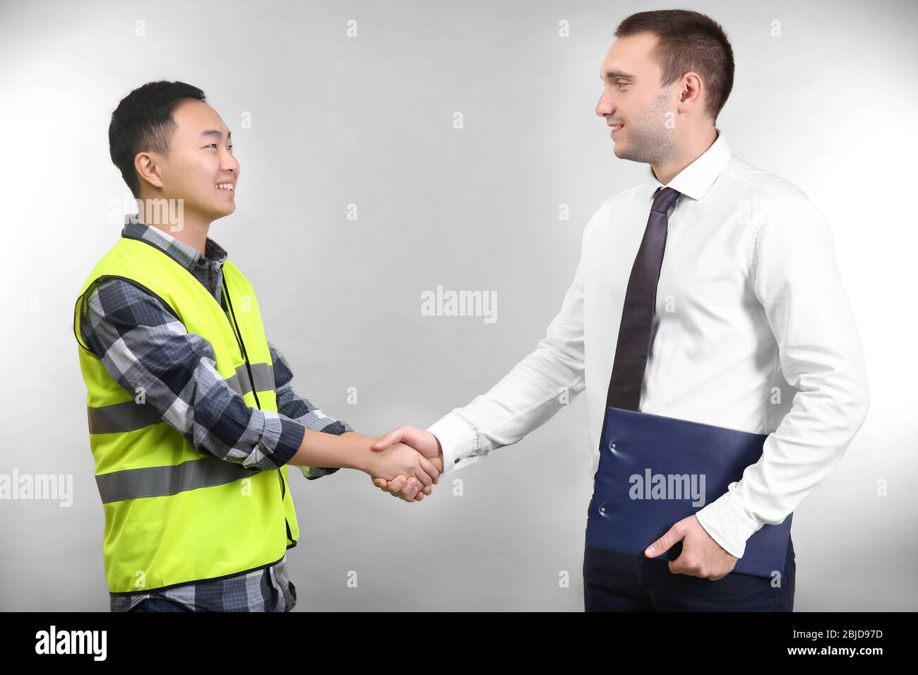 Handsome man shaking hands with warehouse worker, on light background ...