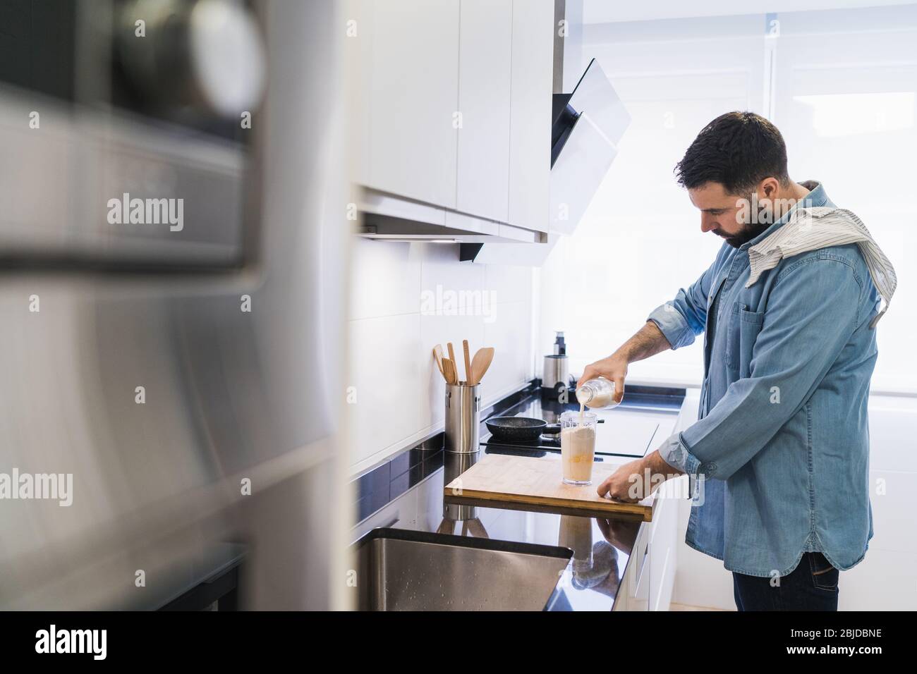 Man cooking in the kitchen in a denim shirt. A man is pouring milk into ...